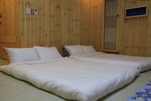 Uma cama de casal com roupa de cama branca em um quarto com paredes de madeira e uma pequena prateleira.