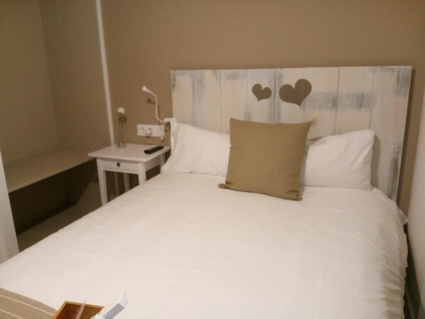 Cama bem arrumada com edredom branco e duas almofadas, uma bege e outra branca.