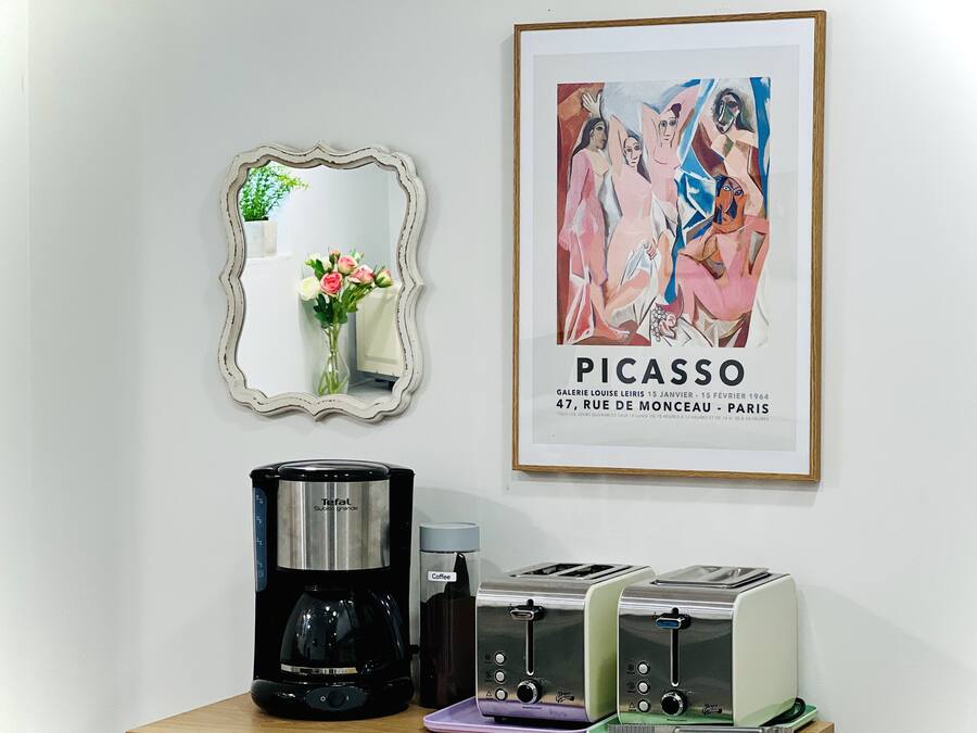 Uma obra de arte de Picasso emoldurada, uma cafeteira, uma torradeira e um espelho com um vaso de flores.