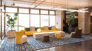 Um lobby moderno com um sofá amarelo, um tapete estampado e uma grande janela.