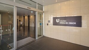 Entrada moderna de hotel com porta de vidro, placa indicando 'VIA INN SHINAGAWA OIMACHI' e piso ladrilhado.