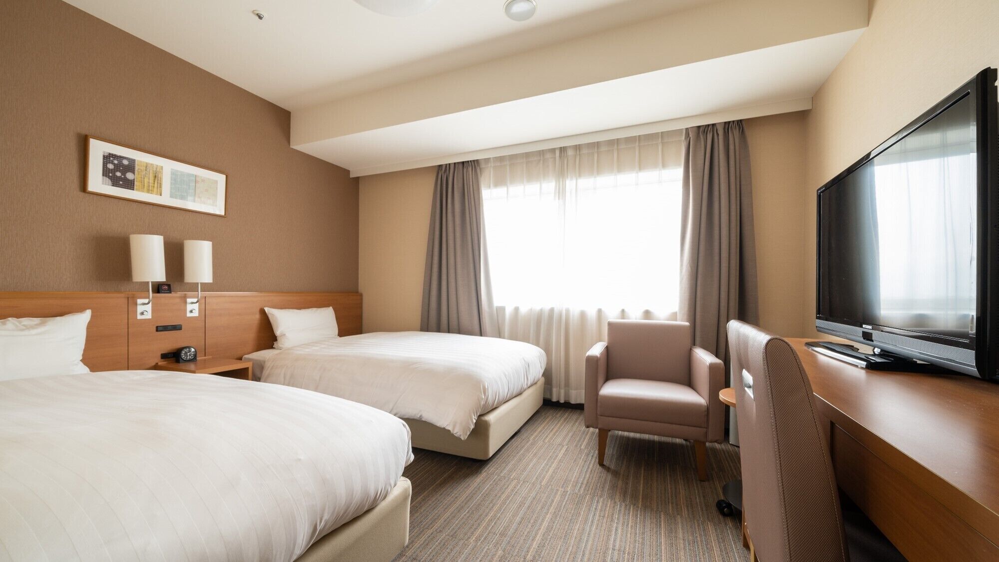 Quarto de hotel com duas camas, televisão, cadeira, escrivaninha e janela com cortinas.