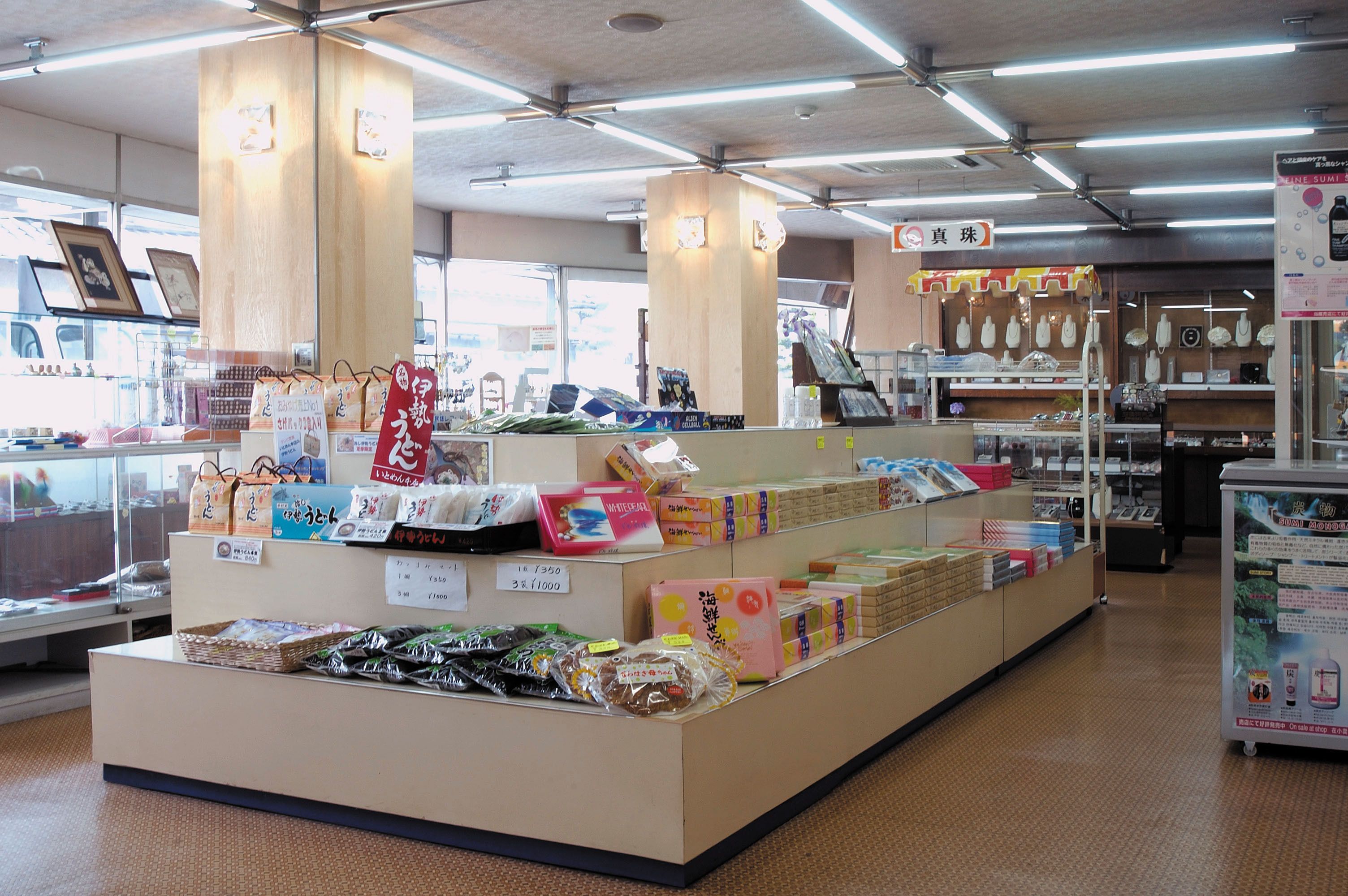 Interior de loja com prateleiras repletas de produtos embalados, balcão de exposição com itens promocionais e área de pagamento visível.