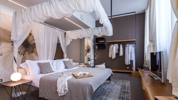 Quarto moderno com cama grande, mesas de cabeceira, abajur, televisão e guarda-roupa.