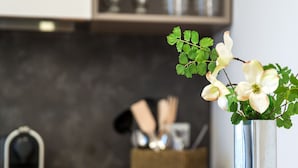 Uma bancada de cozinha com uma xícara branca, um copo e um vaso de metal com flores.