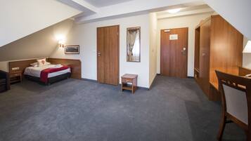 Quarto de hotel com uma cama, uma escrivaninha, uma mesinha e dois guarda-roupas.