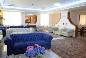 Uma sala de estar ampla com um sofá azul, poltronas brancas e um tapete estampado.
