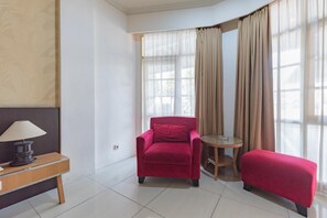 Quarto moderno com uma poltrona vermelha, uma mesinha redonda e um banquinho combinando.