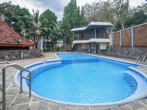 Piscina com deck de pedra, rodeada por um muro de pedra e um edifício com telhado de telhas vermelhas.