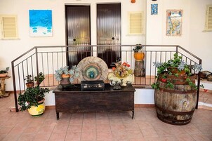 Um banco de madeira com objetos decorativos e plantas em vasos num pátio com grades de metal e portas ao fundo.