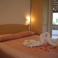 Quarto de hotel com cama, luminária fixada na parede e porta que dá para o exterior.