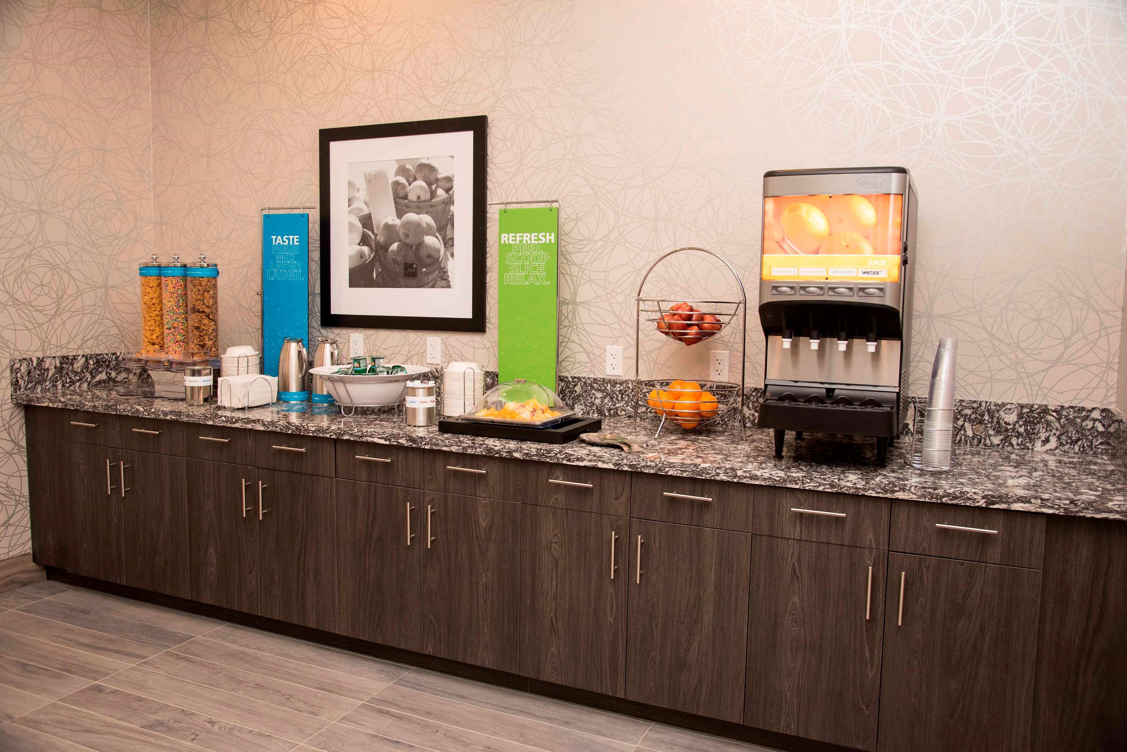 Uma cozinha com bancada de mármore, máquina de café, dispensador de frutas e um quadro na parede.