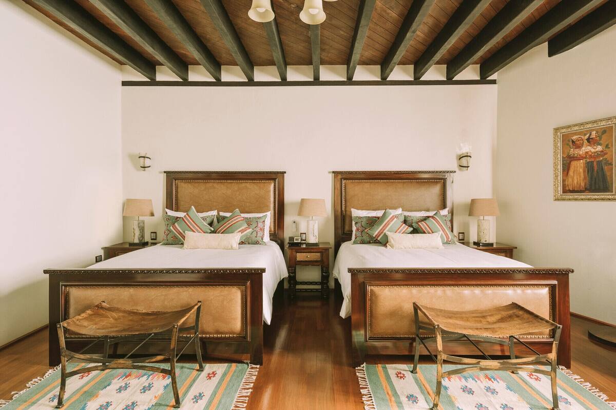 Quarto com cama de casal, duas mesas de cabeceira, teto de madeira e tapete estampado.