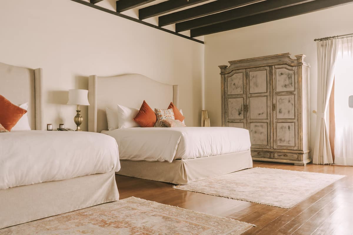 Quarto de hotel com duas camas, um armário de madeira grande e uma janela ampla com cortinas.