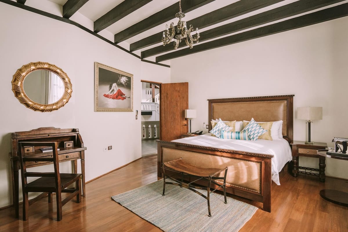 Um quarto com cama de madeira, espelho, escrivaninha e lustre.