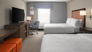 Quarto de hotel com televisão de tela plana, duas camas, uma escrivaninha, uma cadeira e uma janela com cortina estampada.