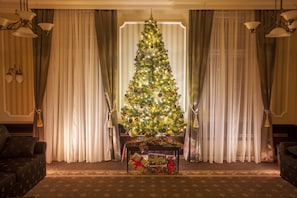 Uma sala de estar com árvore de Natal, sofá, mesa com presentes e cortinas.
