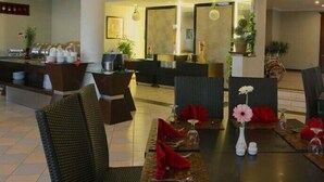 Um hall de hotel com balc ão de recepção, área de estar com mesas e uma parede decorativa.