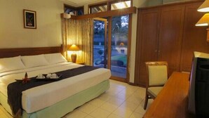 Quarto de hotel com uma cama grande, uma escrivaninha, uma cadeira e vista para o exterior através de uma porta de vidro.
