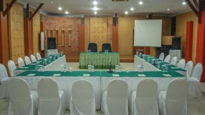 Uma sala de conferências com uma mesa comprida, cadeiras brancas e uma tela de projetor.