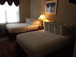 Quarto de hotel com duas camas de solteiro, uma mesa de cabeceira com abajur e um quadro pendurado na parede.