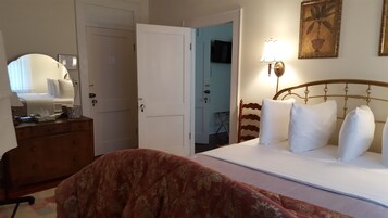 Quarto de hotel com cama, penteadeira, espelho, televisão e abajur.