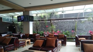 Um hall amplo com sofás de couro e mesas, uma TV de tela plana na parede, e uma parede de pedra com plantas.
