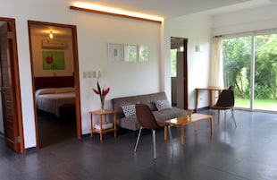 Uma sala de estar moderna com um sofá, cadeiras, uma mesa de centro e uma cama ao fundo.