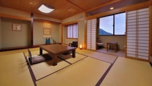 Um quarto japonês tradicional com tatames, uma mesa de madeira, portas deslizantes e vista para uma montanha.