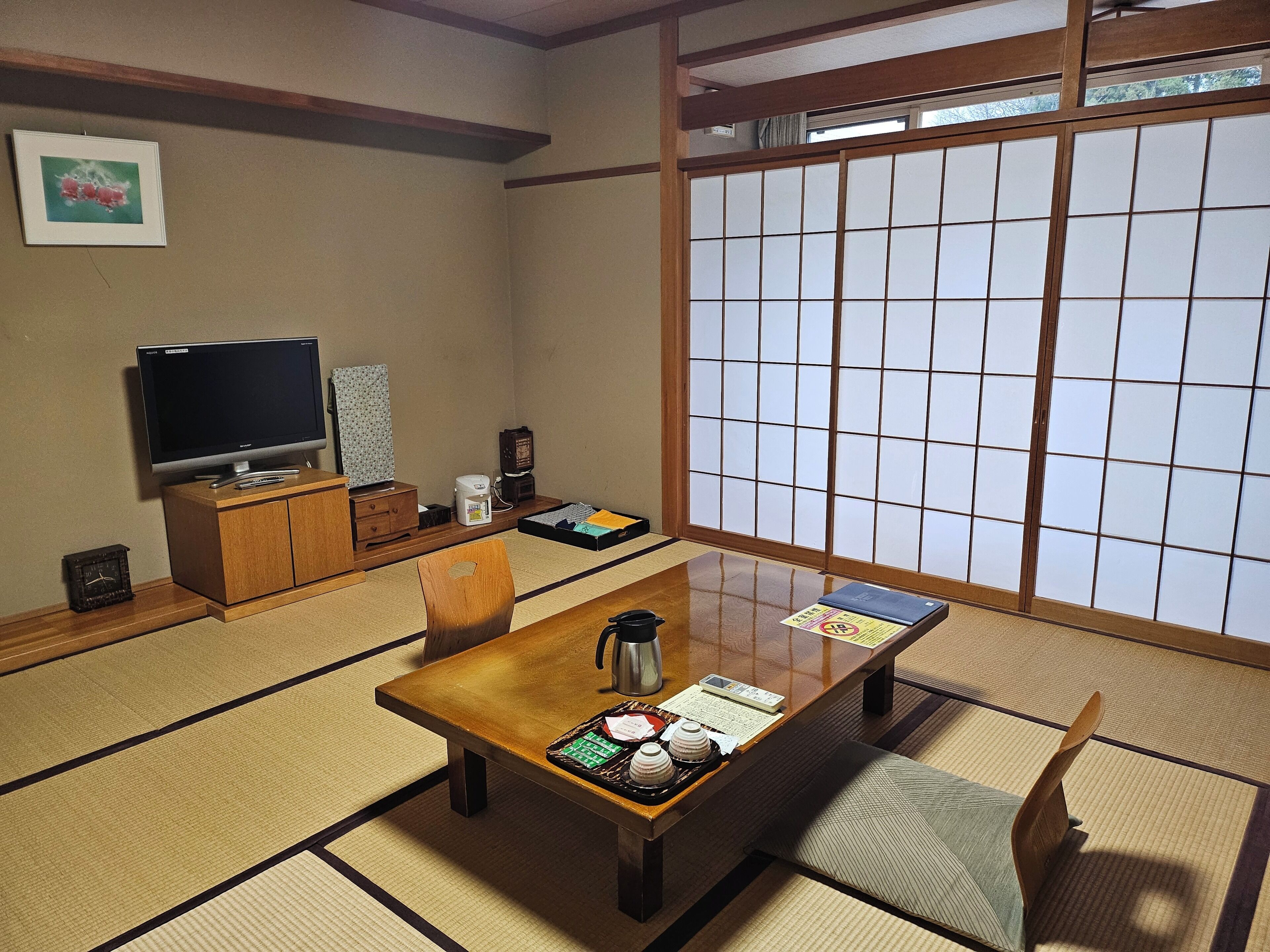 Um quarto japonês tradicional com tatames, uma mesa baixa com um tabuleiro de objetos, uma televisão e portas deslizantes.