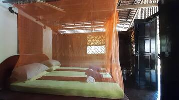 Quarto com cama coberta por um mosquiteiro, janela com grades e porta.