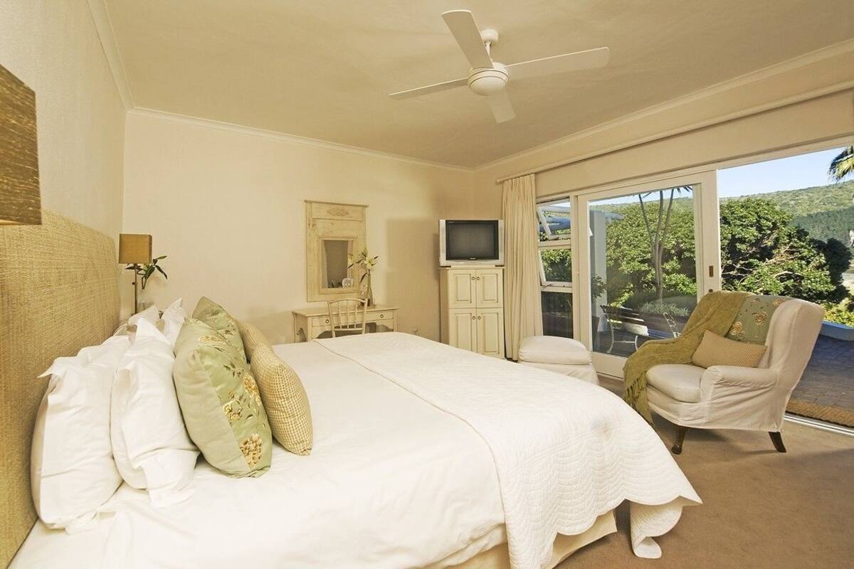 Quarto com cama grande, uma cadeira, televisão e vista para o exterior.