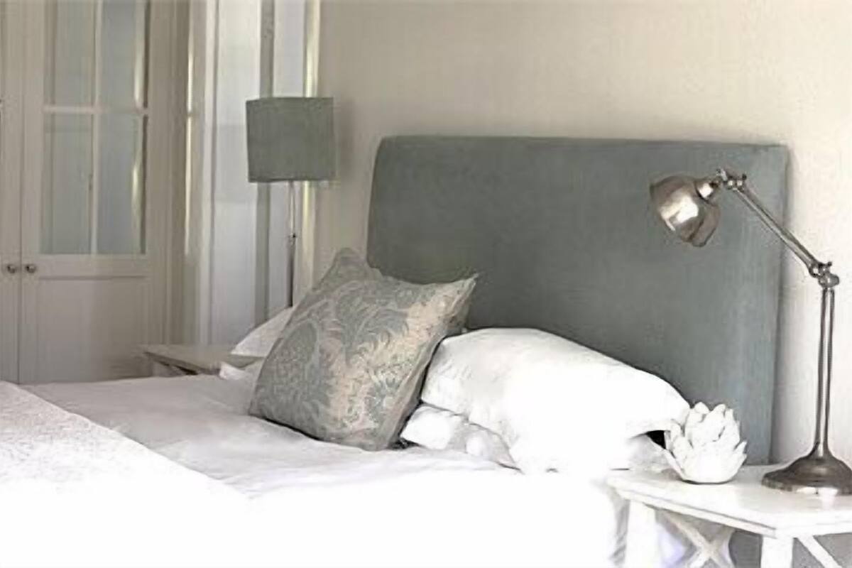Quarto com cama, mesa de cabeceira, abajur e porta.