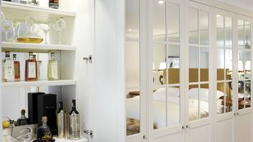 Quarto de hotel com minibar, cama com lençóis brancos e um espelho grande refletindo o ambiente.