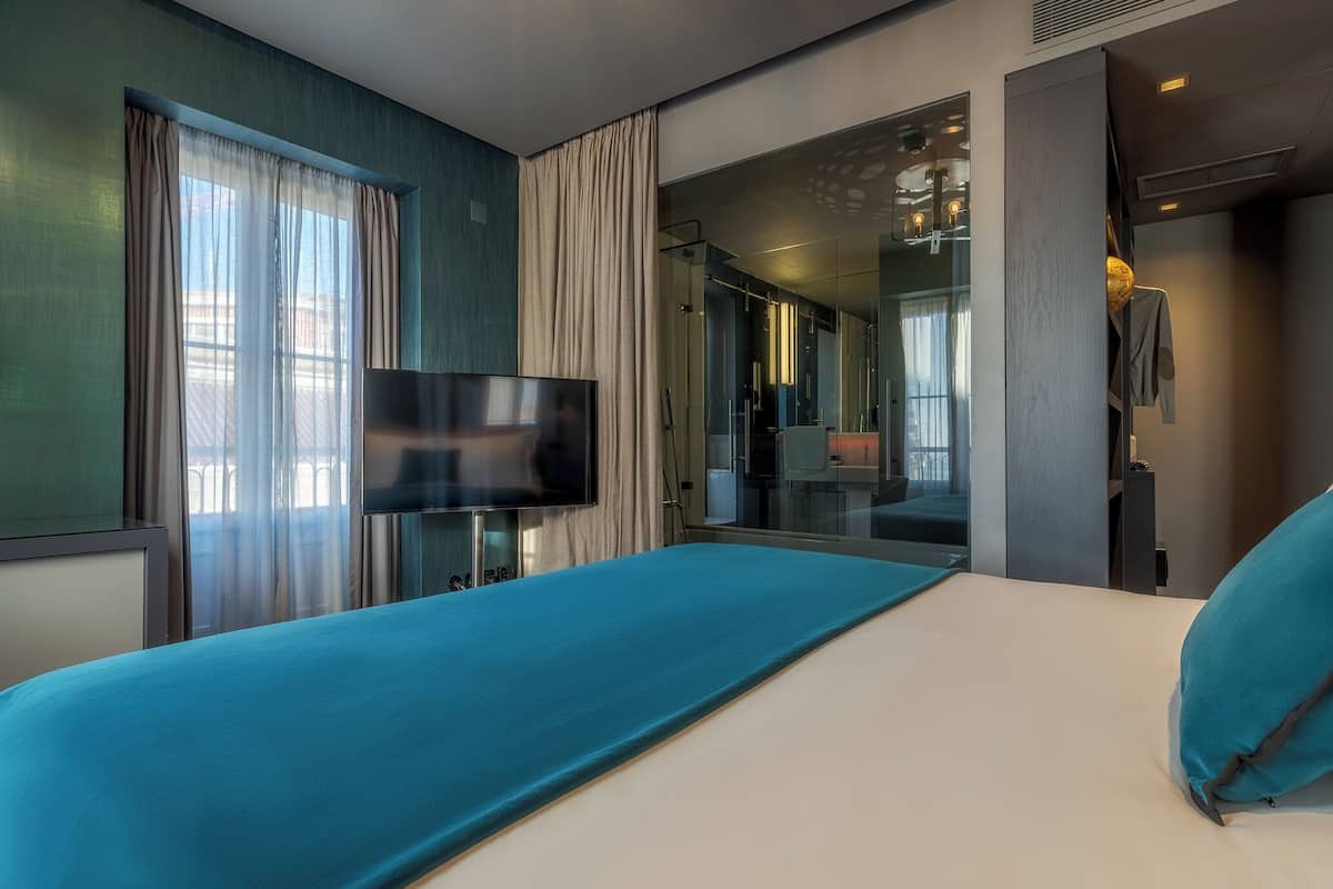 Quarto de hotel moderno com uma cama grande, televisão de tela plana e um espelho amplo.