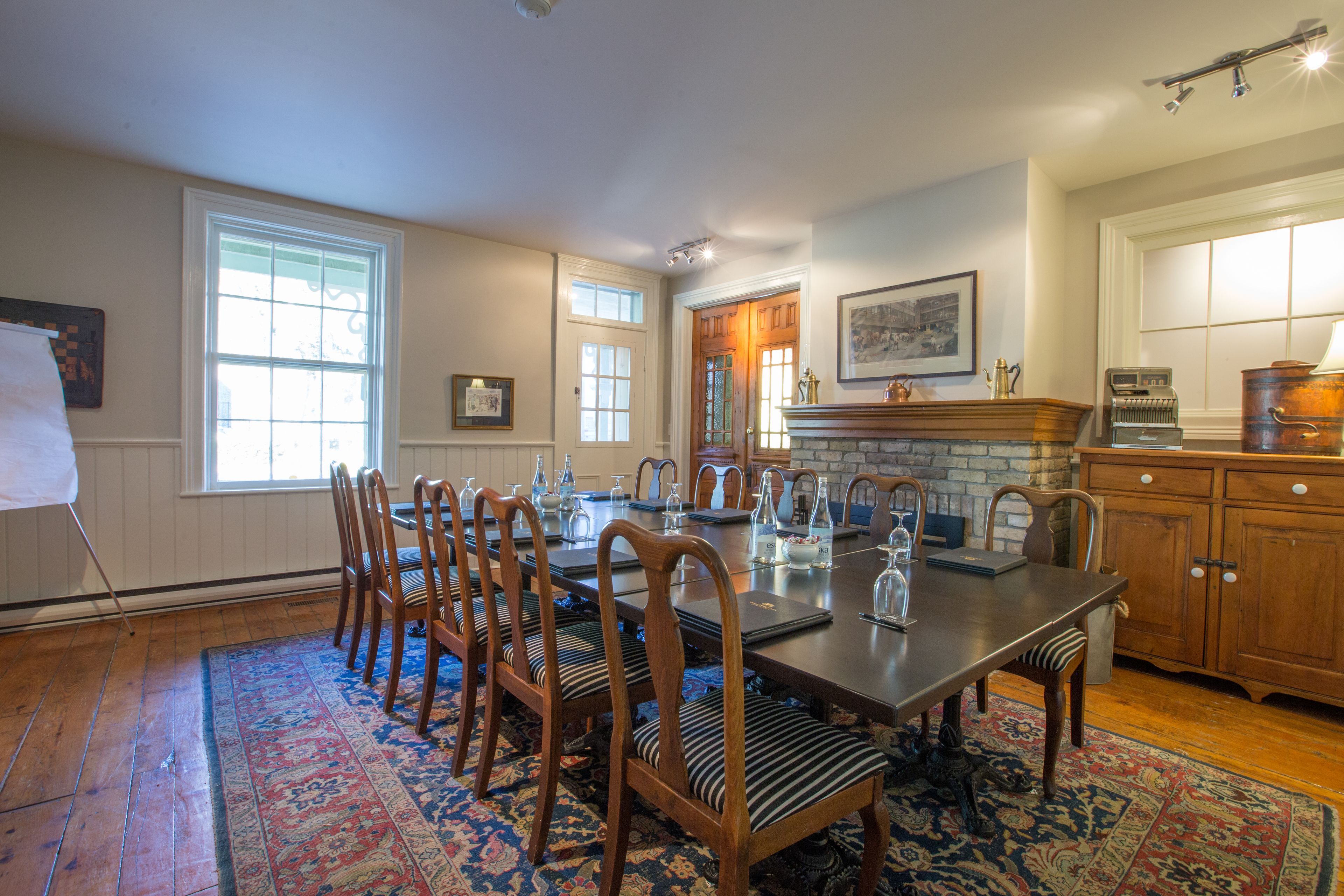 Uma sala de jantar com uma mesa de madeira comprida, cadeiras e um tapete estampado.