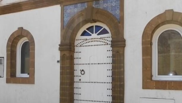 Um edifício com uma grande porta branca, duas janelas em arco e um padrão decorativo de azulejos sobre a porta.