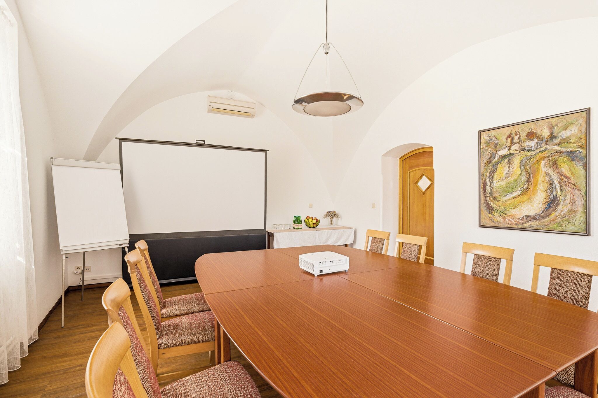 Uma sala de conferências com uma mesa comprida, cadeiras, um projetor, um quadro branco e um quadro na parede.