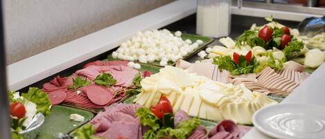 Buffet com diversos queijos, carnes e acompanhamentos.