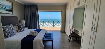 Quarto de hotel com cama, escrivaninha, televisão e varanda com vista para o mar.
