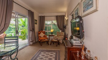 Uma sala de estar acolhedora, com uma TV grande, assentos confortáveis e vista para o verde lá fora.