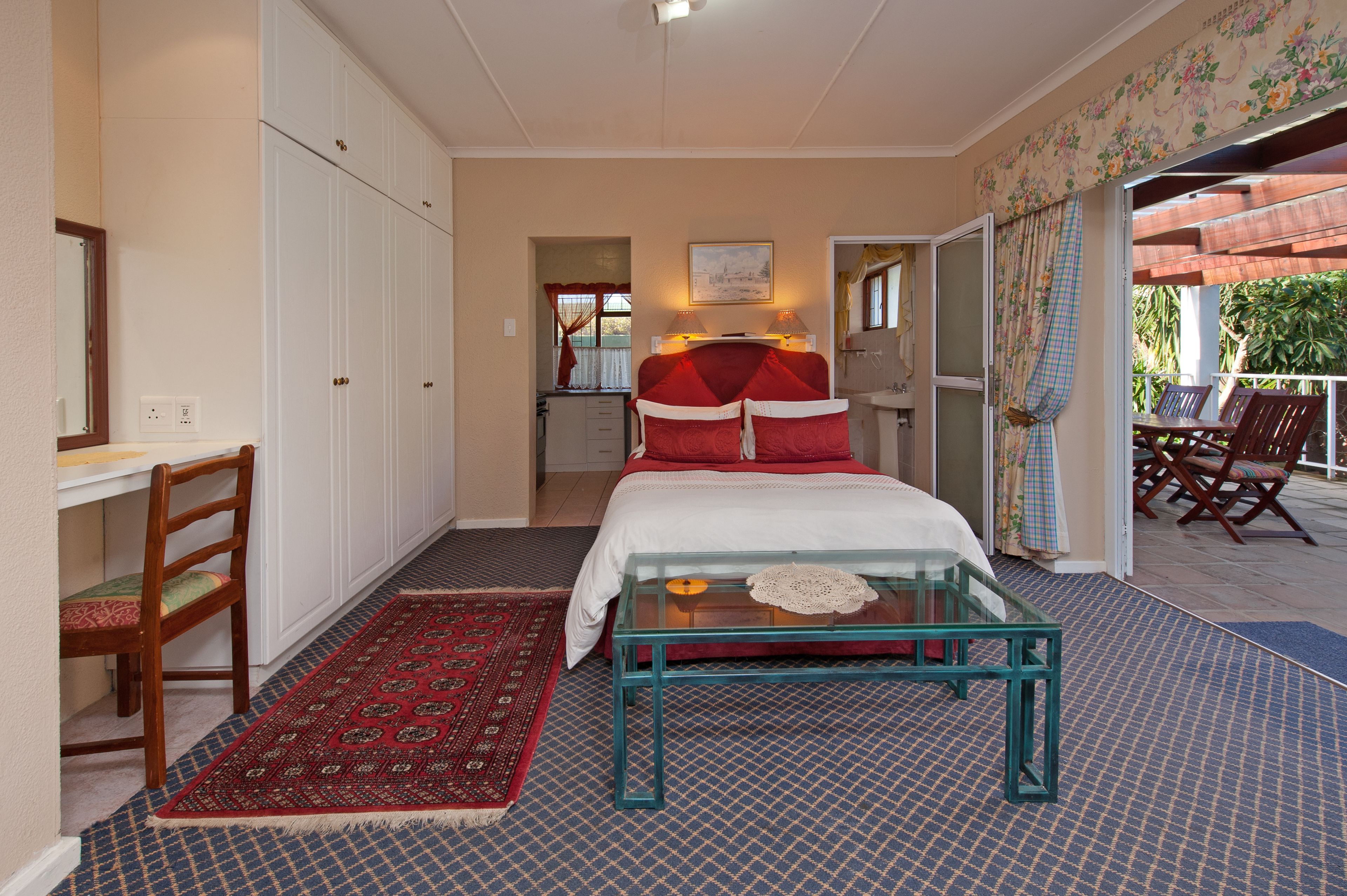 Quarto com cama, escrivaninha, cadeira, mesa de centro de vidro e tapete estampado.