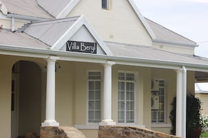 Um edifício com uma placa que diz "Villa Beryl" sobre a entrada, colunas brancas e persianas nas janelas.