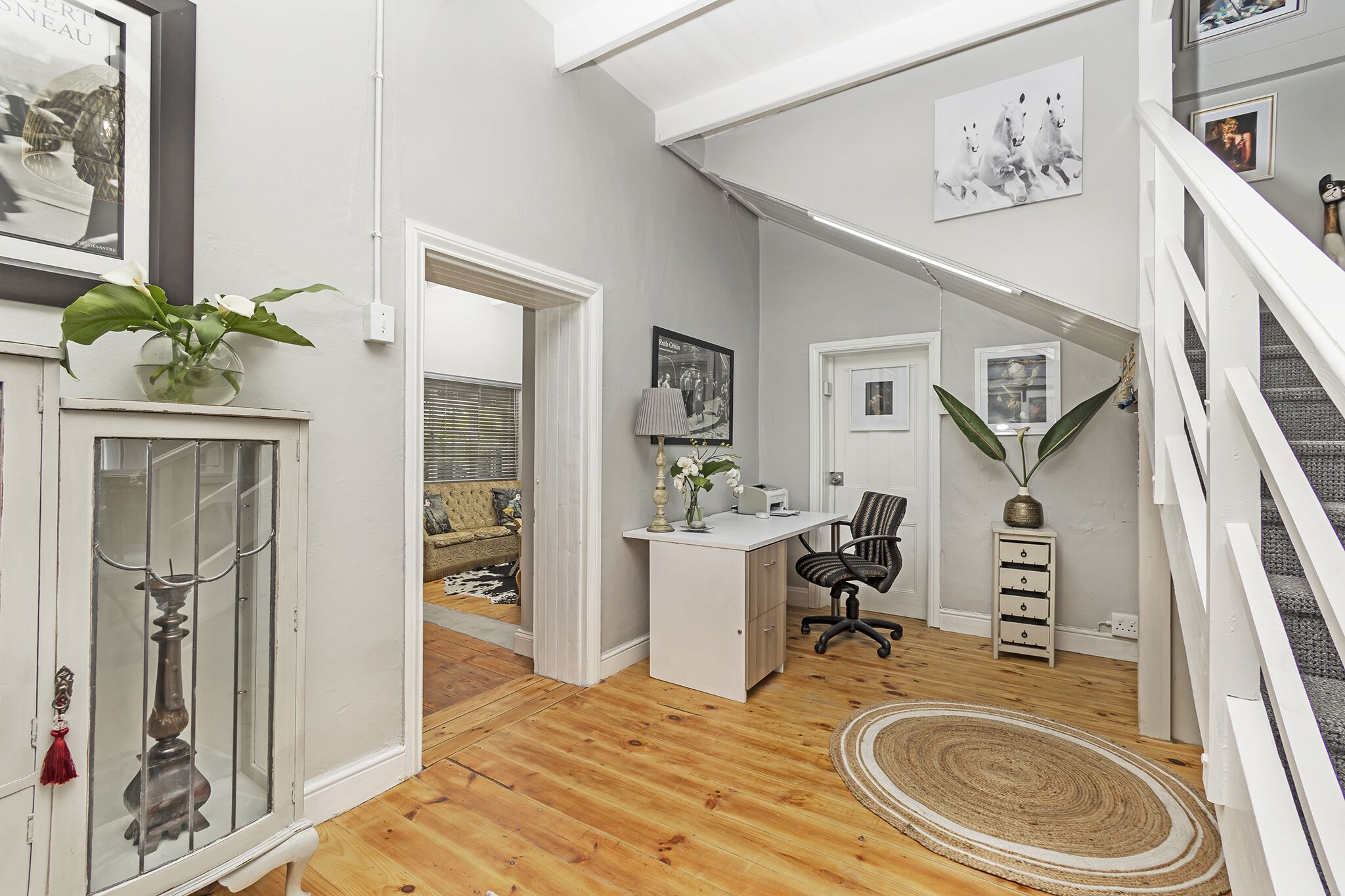 Quarto amplo com piso de madeira, uma escrivaninha com cadeira, uma planta em vaso e uma escada.