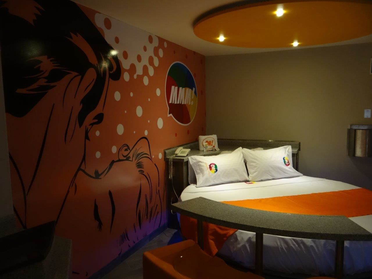 Quarto de hotel com cama, um mural na parede e luminária no teto.
