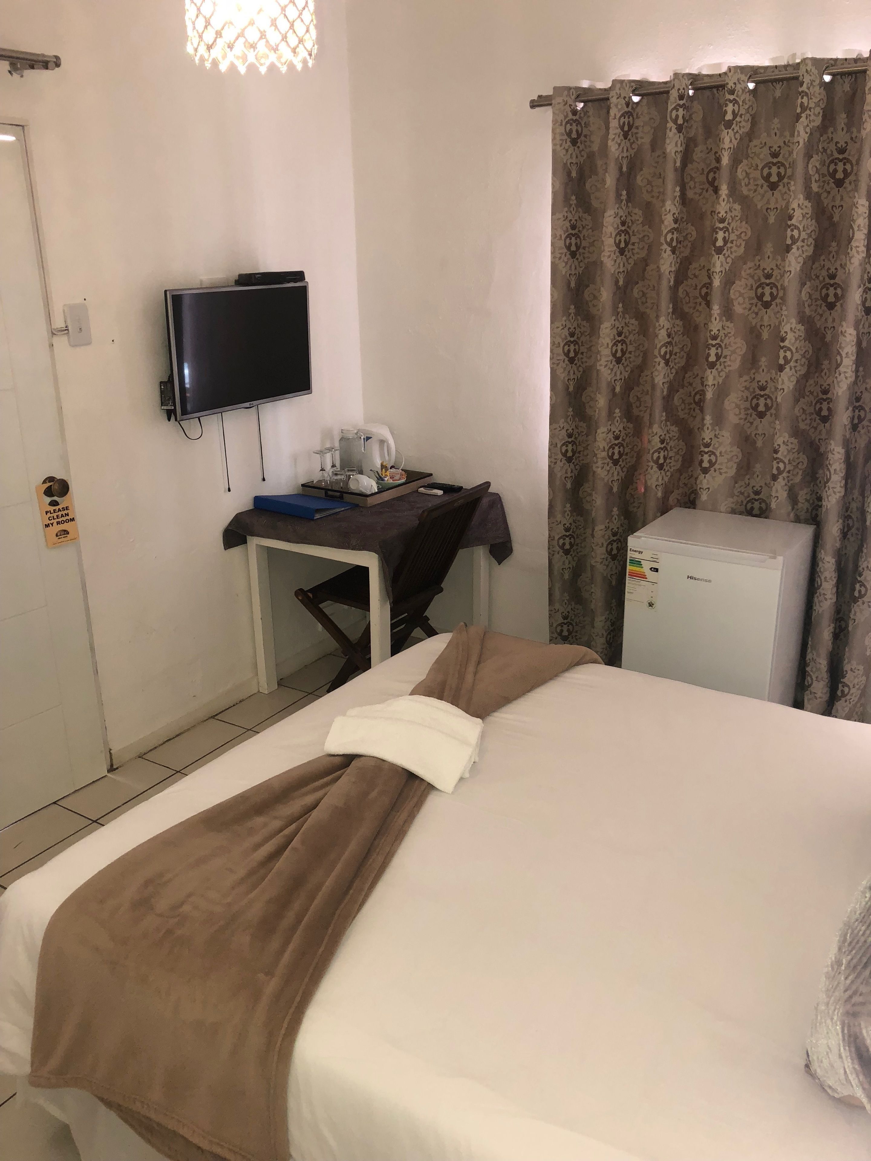 Quarto de hotel com uma cama, uma escrivaninha com televisão, um frigorífico e uma cortina.