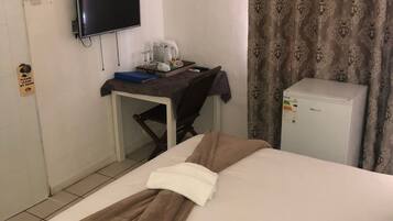 Quarto de hotel com uma cama, uma escrivaninha com televisão, um frigorífico e uma cortina.