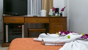 Quarto de hotel com uma cama, televisão sobre uma cômoda de madeira, uma mesa pequena e um armário.