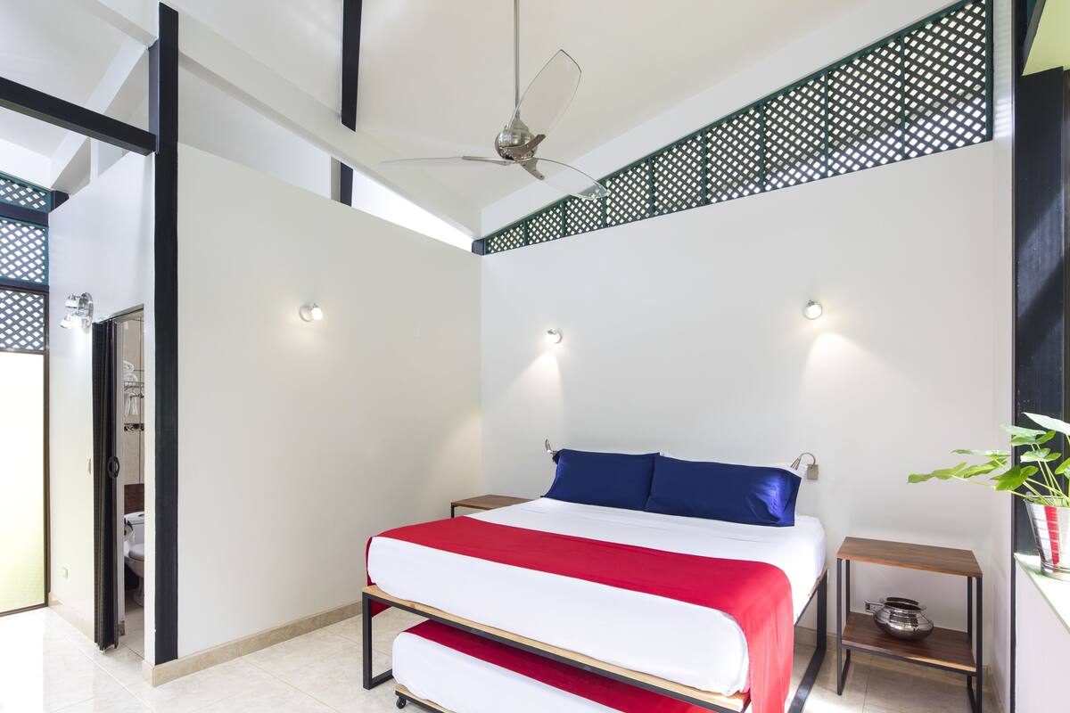 Quarto moderno com cama, mesas de cabeceira, ventilador de teto e um painel decorativo.