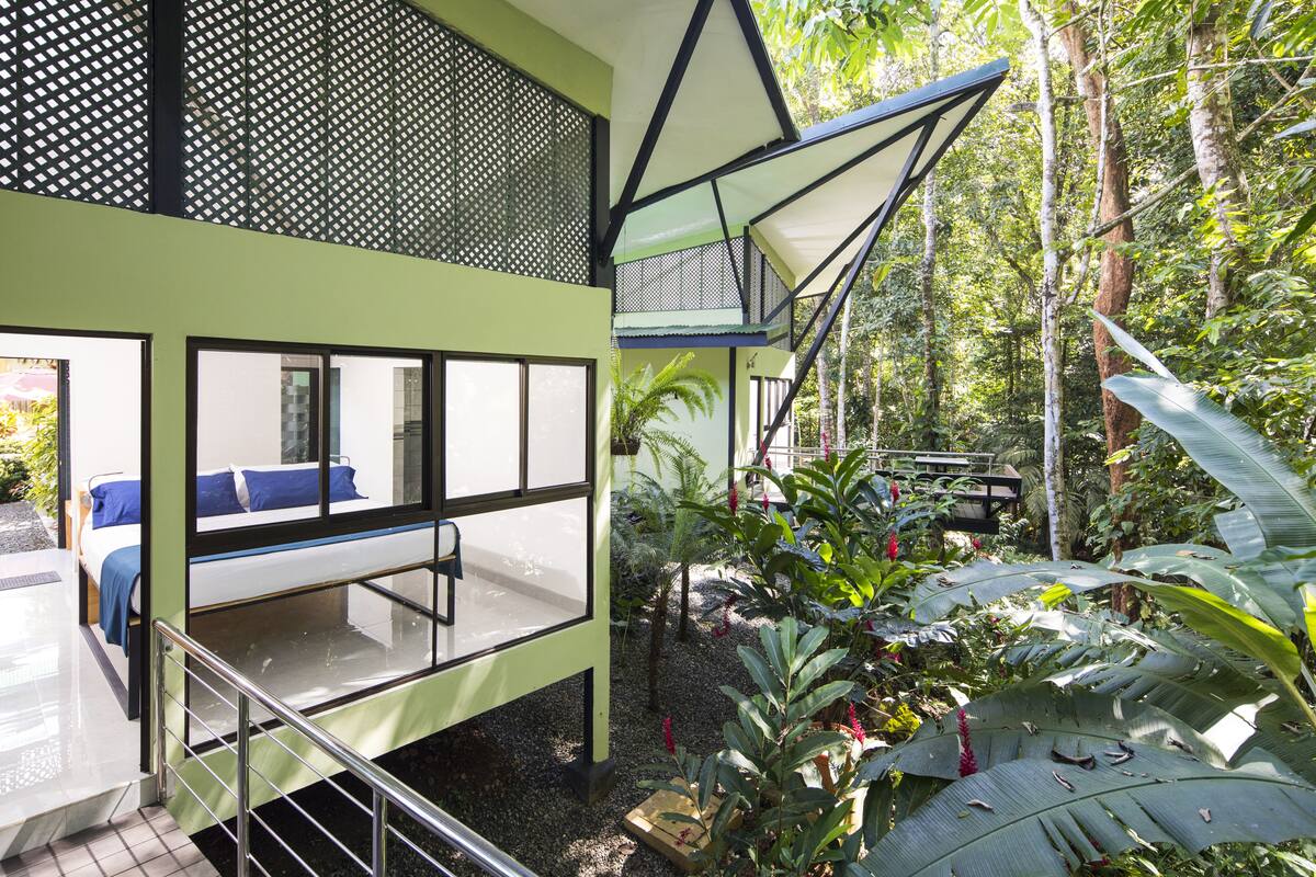 Quarto de hotel moderno com uma cama grande, varanda e vista para o verde ao redor.